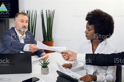 두 명의 남성 동료 사이의 현대 경색 사무실 테이블에 앉아 종이 보고서를 주고 젊은 아프리카 사업가의 클로즈업 샷을 잘라 비즈니스 미팅 브레인스토밍 교육에 대한 스톡 사진