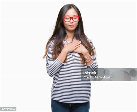 젊은 아시아 여자와 웃 고 고립 된 배경 위에 안경이 닫힌된 눈과 얼굴에 감사 제스처와 함께 가슴에 손 건강 개념입니다 감사에