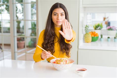 젊은 여자는 아시아 쌀의 그릇을 먹는 젓가락을 사용 하 여 열린 손으로 중지 표시를 심각 하 고 자신감 있는 표현 국방 제스처 가정 생활에 대한 스톡 사진 및 기타 이미지