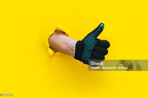검은색 천으로 된 작업용 장갑을 낀 왼쪽 남자의 손은 엄지손가락을 치켜들고 있다 노란 종이에 작은 찢어진 구멍 좋은 직업 재미있는 분위기 및 승인 개념 공간을 복사합니다
