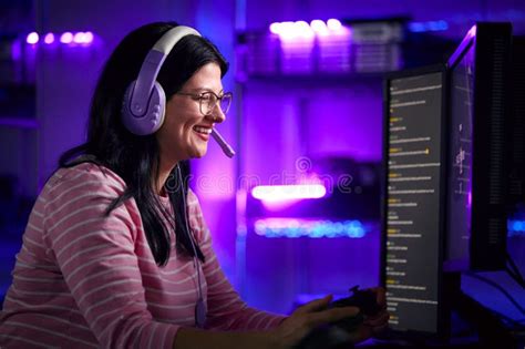 Low Key Lighting Shot Of Female Gamer In Front Of Computer Screens With Headphones And