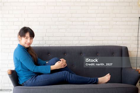 아름 다운 초상화 젊은 아시아 여자 앉아서 웃 고 행복 하 고 거실에서 캐주얼 소파에 카메라를 보고 명랑 하 고 집에서 소파에 휴식 라이프 스타일 개념 가정 생활에 대한