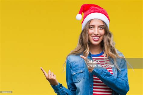 아름 다운 젊은 금발 여자 웃 고 옆에 두 손과 손가락으로 가리키는 카메라 보고 격리 된 배경 위에 크리스마스 모자를 쓰고 가리키기에 대한 스톡 사진 및 기타 이미지