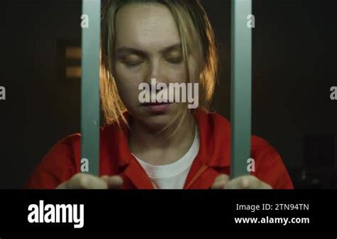 Female Prisoner In Orange Uniform Shakes Holds Metal Bars Looks At