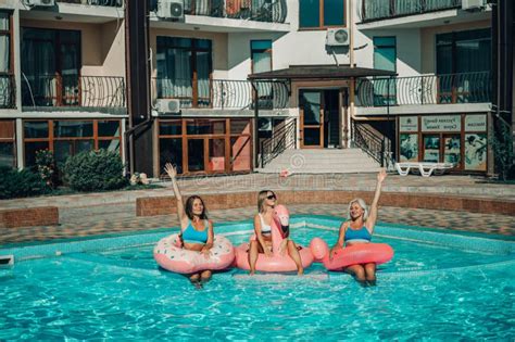 Three Women Are Sitting On Inflatable Floats In A Pool Scene Is Lighthearted And Fun Stock