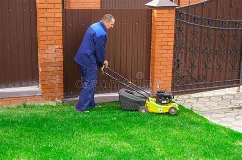 The Man Is Working In The Garden Mowing Grass With A Lawn Mower Stock