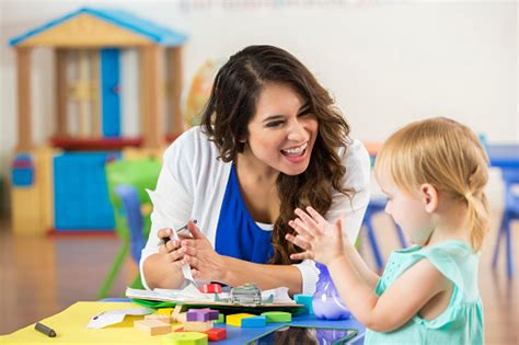 Hispanic Teacher Praises Cute Preschooler In Daycare Classroom Stock