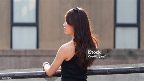 화창한 날에 회색 건물 배경으로 포즈를 취하는 긴 검은 머리를 가진 우아한 젊은 여성 트렌디 한 여름 섹시한 블랙 드레스 백라이트 여름 개념에 멋진 중국 여자의 야외 초상화