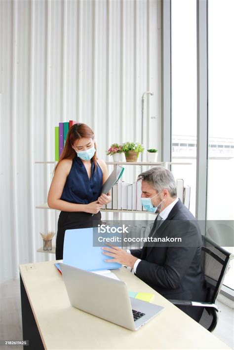 아시아계 여성 사업가 또는 비서가 마스크를 착용하고 나이 든 고위 백인 관리자에게 문서를 보내 사무실에서 프로젝트 작업에 서명하도록 합니다 25 29세에 대한 스톡 사진 및