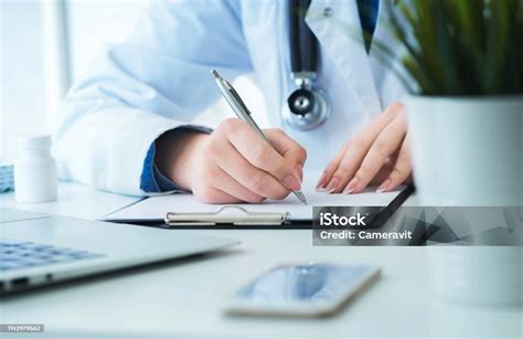 여성 의사는 병원 근접 촬영에서 책상에 앉아있는 동안 신체 검사 또는 질병 예방 중에 클립 보드 패드에서 처방전 양식이 나 환자 역사 목록을 작성 개념에 대한 스톡 사진 및