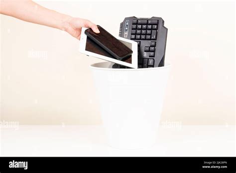 Female Hand Puts Used Digital Tablet Computer And Cell Phones Into Recycling Bin Full Of Old