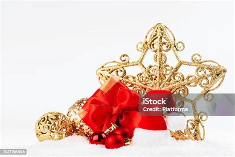 공간을 복사합니다 빨간 활로 묶인 새해 선물은 크리스마스 트리의 금빛 별 옆에 있으며 산타의 모자와 새해의 빨간색과 금색 반짝이는 공이 밝은 배경의 눈 위에 놓여 있습니다