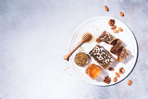 꿀 제품 배경입니다 벌집 프레임 꿀벌 꽃가루 과립 유리 냄비에 꿀 회색 콘크리트 배경에 아몬드 너트 공간을 복사합니다 맨 위 보기 가을 수확 개념입니다 배너 0명에 대한