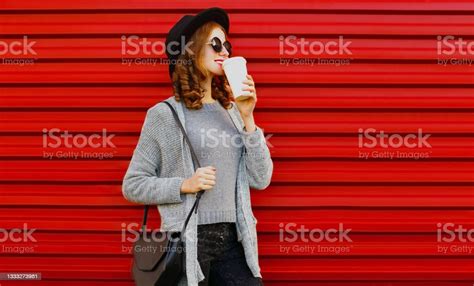 검은 둥근 모자를 쓰고 커피 한 잔을 들고 있는 아름다운 젊은 여성의 초상화 빨간색 배경에 회색 니트 스웨터 20 29세에 대한 스톡 사진 및 기타 이미지 Istock