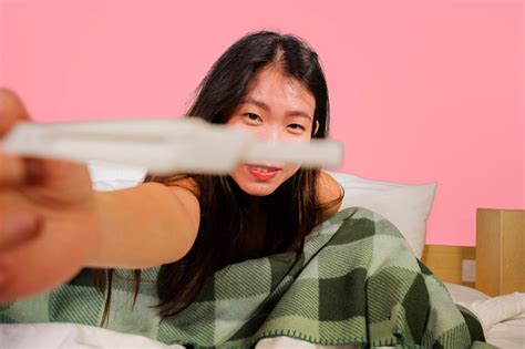 젊은 행복 하 고 흥분 아시아 한국 여성 임신 테스트 검사를 들고 침대에 놀란 황홀 하 고 즐거운 기대 아기 축복 느낌의 기