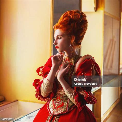 밝은 배경에 역사적인 헤어스타일으로 젊은 동화 로코코 여왕 초상화 붉은 머리를 가진 르네상스 공주입니다 빨간 역사적인 복장에