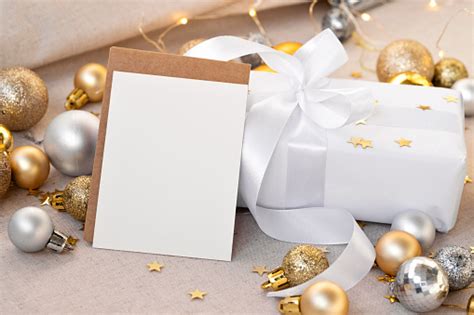 빈 종이 카드 모형 봉투 화이트 크리스마스 새해 또는 생일 선물 상자 금색과 은색 장식 공 베이지 색 테이블 배경에 별 색종이 조각 명절 선물 및 엽서 템플릿 크리스마스