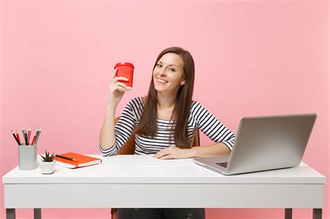 커피 또는 차 프로젝트 파스텔 핑크 배경에 고립 된 Pc 노트북으로 사무실에 앉아 들고 성공적인 여자 성과 비즈니스 경력 개념입니다 광고에 대 한 공간을 복사 합니다 갈색