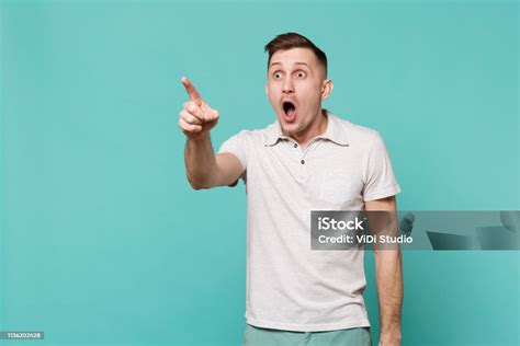 입이 열린 입을 유지 캐주얼 의류에 충격 젊은 남자 지시 검지 손가락 따로 스튜디오에서 파란색 청록색 벽 배경에 고립 사람들은 진심으로 감정 라이프 스타일 개념입니다 복사