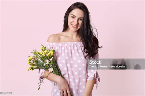 밝고 어두운 머리 여자의 고립 된 총 폴카 도트 여름 드레스를 입고 꽃의 꽃다발을 보유 하 고 꽃을 좋아하는 3 월 8 일을 기념 맨 손으로 어깨를 보여줍니다 그리고 행복을