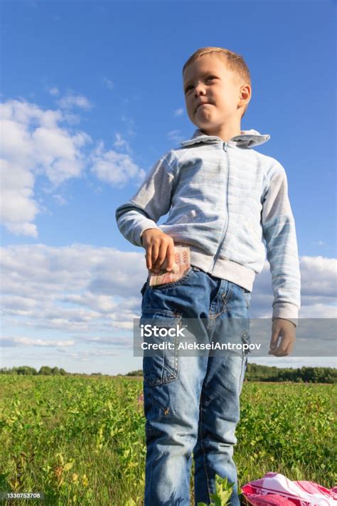 청바지와 스웨터를 입은 만족스러운 미취학 아동은 구름이 있는 푸른 하늘을 배경으로 들판에서 종이 돈을 들고 있습니다 6 7 살에 대한 스톡 사진 및 기타 이미지 Istock