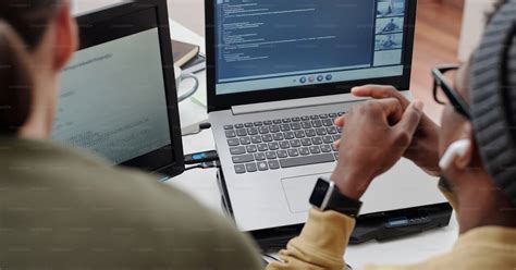 여성 동료 옆에 직장에 앉아 있는 동안 화면에 화상 채팅이 있는 노트북의 키패드 위에 있는 젊은 흑인 남성의 손 사진 Unsplash의 노트북 코드 이미지