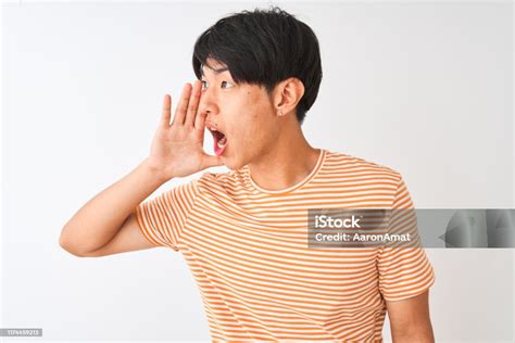 캐주얼 스트라이프 티셔츠를 입은 젊은 중국인 남성이 고립된 흰색 배경 위에 서서 입을 다물로 큰 소리로 외치고 비명을 지르고