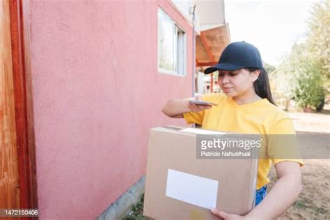 Young Delivery Woman Scanning The Qr Code With Her Mobile From A Cardboard Box Before Delivering