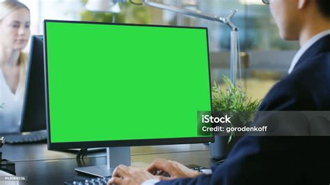 모형 그린 스크린으로 개인용 컴퓨터에 그의 책상에 사무실 사업가 작동 합니다 그의 동료는 그 반대 세트 컴퓨터에 대한 스톡 사진
