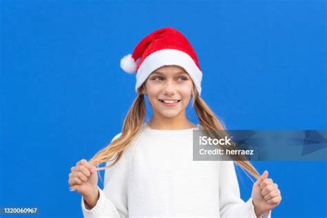 흰색 스웨터와 파란색 배경에 고립 된 멀리 미소 피그 테일을 들고 산타 모자를 기쁘게 소녀 고품질 사진 계절에 대한 스톡 사진 및 기타 이미지 Istock