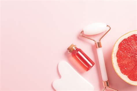 아로마 에센셜 오일 위치 자몽 신선한 슬라이스의 작은 유리 유리 바이알 분홍색 배경에 얼굴 롤러와 과샤 카피 공간이 있는 크리에이티브 트렌디 한 화장품 플랫 레이 0명에