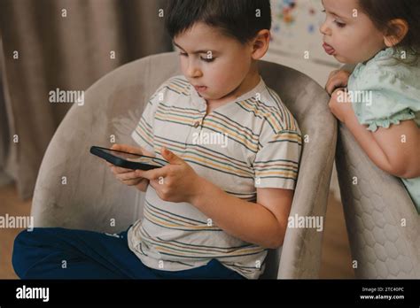 African Brother And Babe Sitting On Armchairs At Home Using Mobile Phone Looking At Device