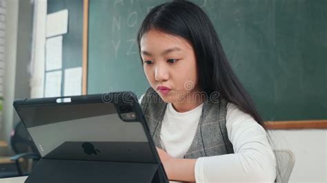 A Girl Wearing Glasses Is Sitting At A Desk With A Tablet In Front Of