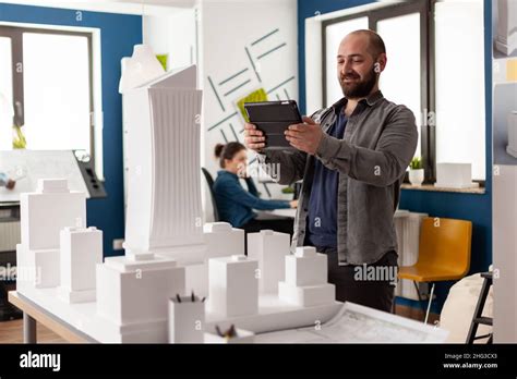 Bearded Professional Architect Looking At Tablet In Front Of White Foam Building Model In