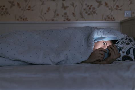 어린 졸린 지친 남자의 초상화는 담요 아래 침대에 누워 늦은 밤에 스마트 폰을 사용하여 불면증 노모 공포증 수면 장애 개념 25 29세에 대한 스톡 사진 및 기타 이미지