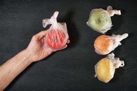 손은 검은 배경에 개별 플라스틱 패키지에 신선한 빨간 토마토를 보유하고 선택하고 과일 개념 환경 오염 문제 또는 건강한 음식을위한 바이러스 보호를 선택 가방에 대한 스톡