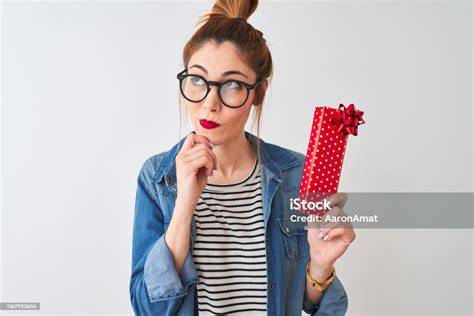 빨간 머리 여자 안경 을 들고 발렌타인 선물 위에 고립 된 흰색 배경 심각한 얼굴 질문에 대 한 생각 매우 혼란 스러운 아이디어 안경에 대한 스톡 사진 및 기타 이미지