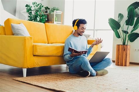 집에서 헤드폰을 끼고 여가 시간을 즐기는 젊은이 자연 채광이 들어오는 아늑한 실내에서 노트북으로 책을 읽고 작업합니다 20 24세에 대한 스톡 사진 및 기타 이미지 Istock