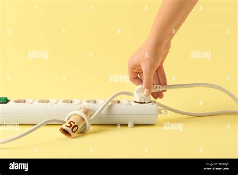 Woman Inserting Plug With Money Into Power Socket On Yellow Background Electricity Bill Concept