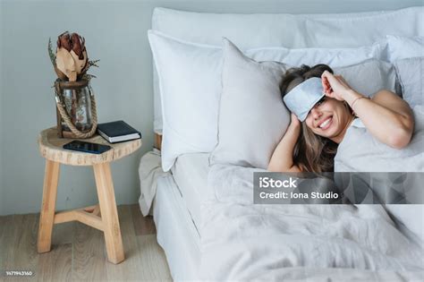 침대에 누워 깨어난 젊은 여자 웃는 백인 소녀는 주말에 집에서 쉬고 있는 장난꾸러기 얼굴 표정으로 수면 마스크를 벗고 밖을