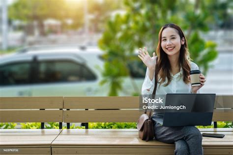 중앙 도시 거리에 앉아있는 트렌디 한 옷을 입은 아시아 곱슬 비즈니스 여성을 웃고 휴대 전화와 노트북을 사용합니다 하얀 셔츠를 입은 예쁜 여름 여자가 거리를 걸어 다니며