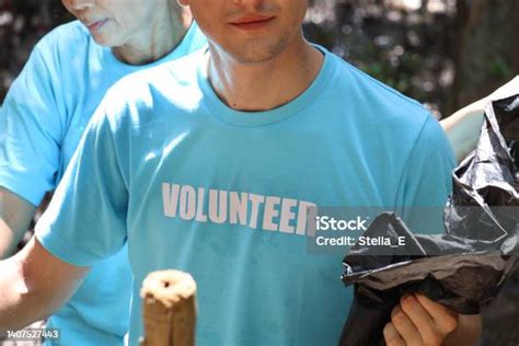 쓰레기 봉투를 들고 파란색 티셔츠를 입고 자원 봉사하고 생태 맨은 토지 오염 환경 문제를 줄이기 위해 쓰레기를 청소하고 집어 들고 세계 환경의 날 2명에 대한 스톡 사진 및