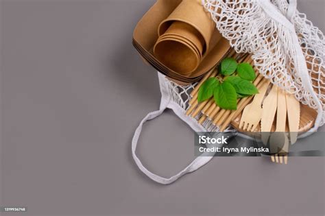 친환경 식기의 클로즈업 복사 공간이있는 밝은 회색 배경에 흰색 면 그물 가방에 나무 칼붙이와 크래프트 종이 식품 컵과 용기 길거리 음식은 종이 포장을 빼앗습니다 감소에 대한