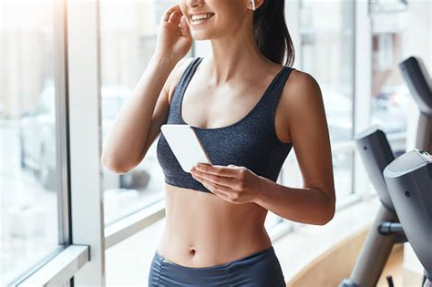 좋아하는 음악을 즐겨 보세요 체육관에 서 있는 동안 그녀의 스마트 폰을 사용 하 여 헤드폰에 젊고 쾌활 한 여자의 잘린 된 이미지 Mp3 플레이어에 대한 스톡 사진 및 기타