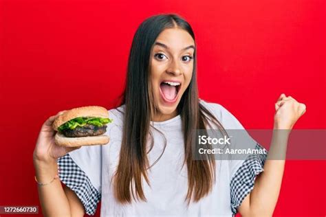 햄버거를 먹는 젊은 히스패닉 여자 자랑 스비 명칭 승리와 성공을 축하 매우 흥분 한 팔 20 24세에 대한 스톡 사진 및 기타 이미지 20 24세 감정 고기 Istock