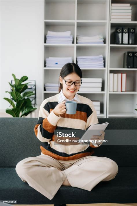 자신감 넘치는 아시아 여성이 거실에서 메모장과 태블릿을 들고 웃으며 집 소파에 서 있다 20 24세에 대한 스톡 사진 및 기타 이미지 20 24세 가상현실 거실