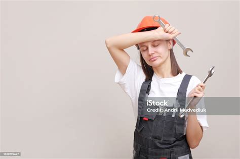 회색 유니폼과 보호 헬멧을 착용한 여성 엔지니어가 도구로 미소를 지으며 손에 렌치를 들고 있다 남성과 여성 사이의 평등 흰