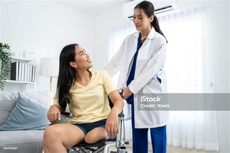 간호사의 지원으로 물리 치료를 받는 아시아 여성 다리 절단 환자 매력적인 어린 소녀 다리가 없는 환자는 집 거실에서 여성 간병인 의사와 함께 보행기 목발을 짚고 천천히 걷는