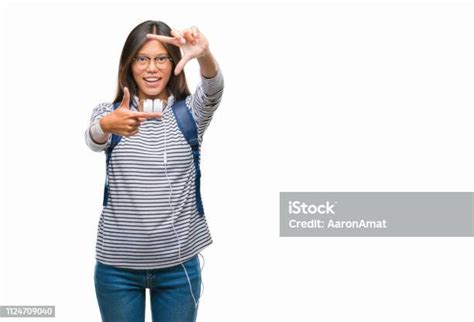 손으로 만드는 프레임 및 행복 한 얼굴로 손가락을 웃 고 고립 된 배경 위에 헤드폰과 배낭을 착용 하는 젊은 아시아 학생 여자 창의력과 사진 개념입니다 가방에 대한 스톡