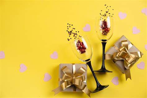 휴일 배경입니다 두 개의 깜박이는 와인 잔 노란색 배경에 분홍색 하트 색종이로 장식 된 다양한 수제 선물 상자 발렌타인 데이 컨셉 플랫 레이 상단 보기 복사 공간 개념에